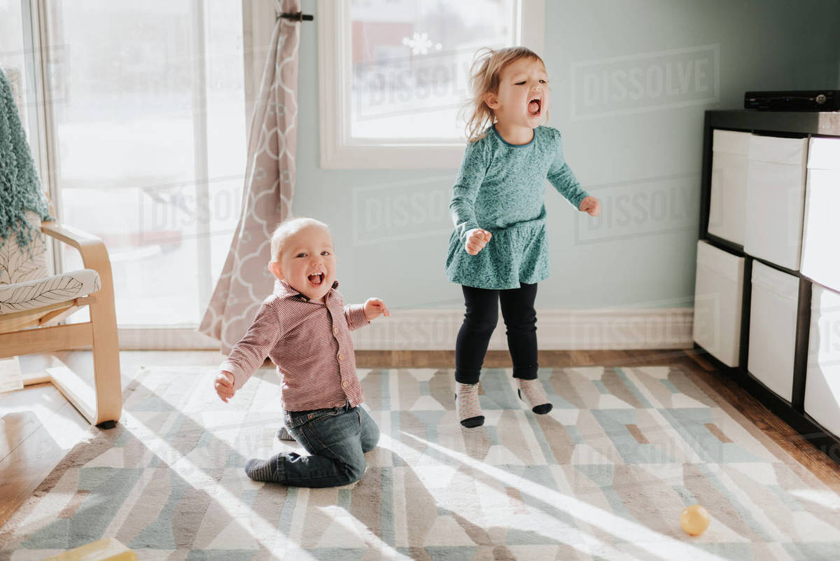 Female toddler and baby brother playing on living room rug - Royalty ...