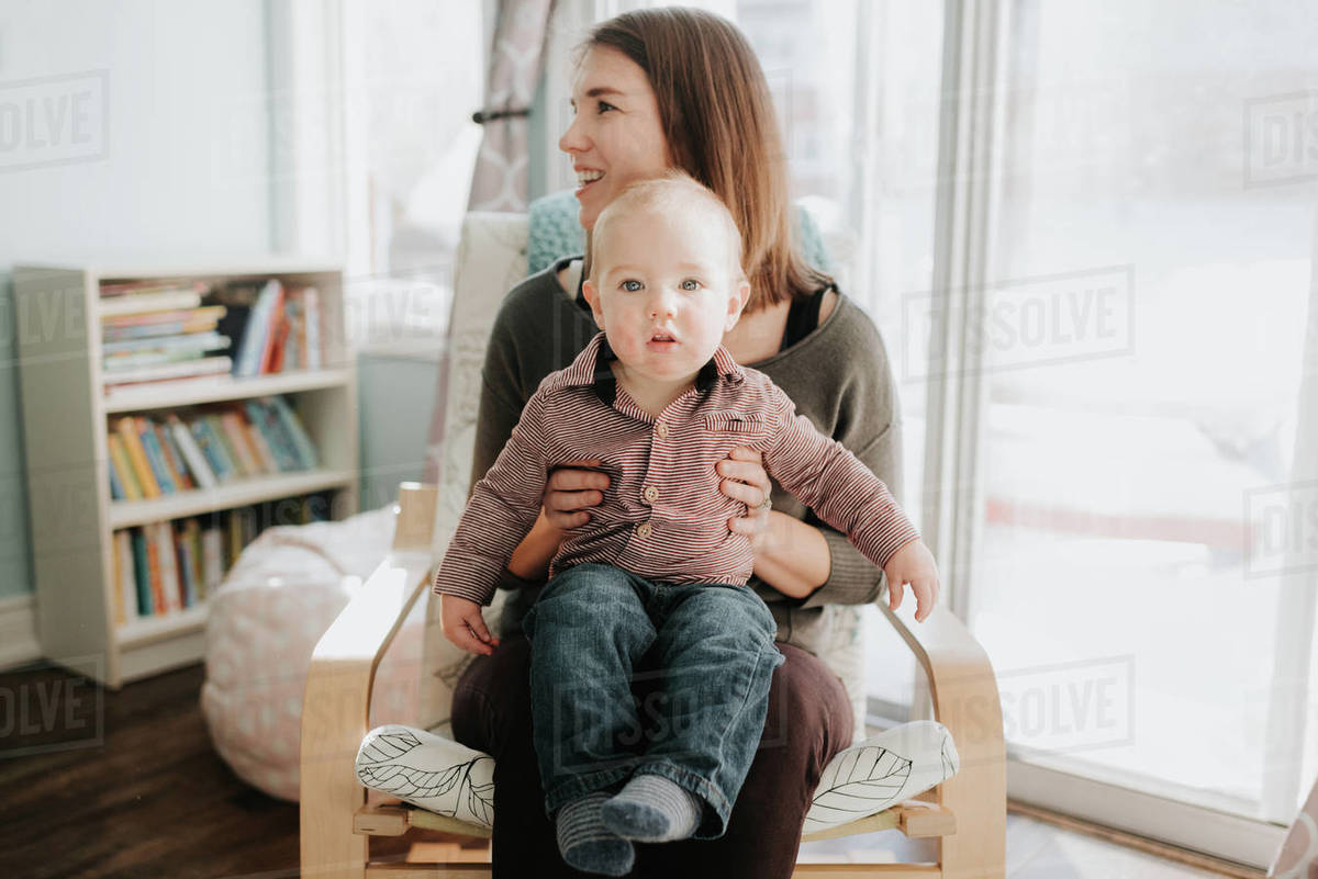Baby boy sitting on mother's lap in living room, portrait - Royalty ...