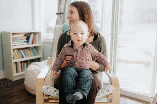 Baby boy sitting on mother's lap in living room, portrait - Royalty ...