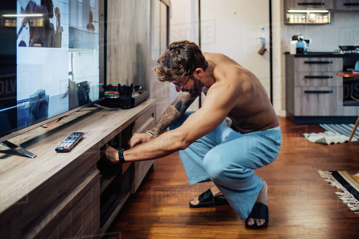 Mid adult man crouching to open living room cupboard - Royalty-free ...