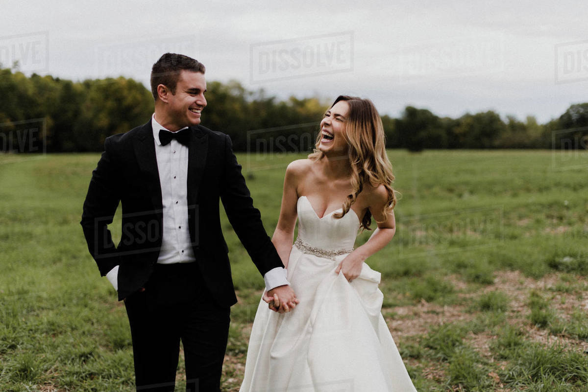 Romantic young bride and groom holding hands and laughing in field ...