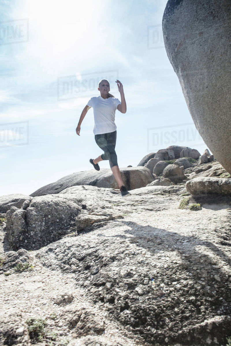 Young female runner running over beach rocks, full length, Cape Town ...