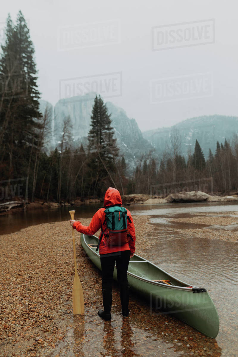 Young female canoeist preparing canoe in river, rear view, Yosemite ...