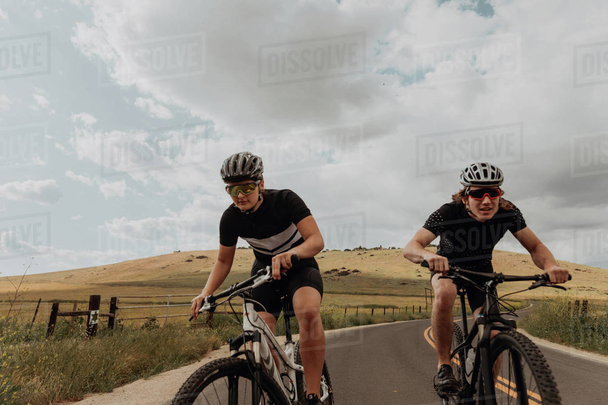 Young cycling couple cycling on rural road, Exeter, California, USA ...
