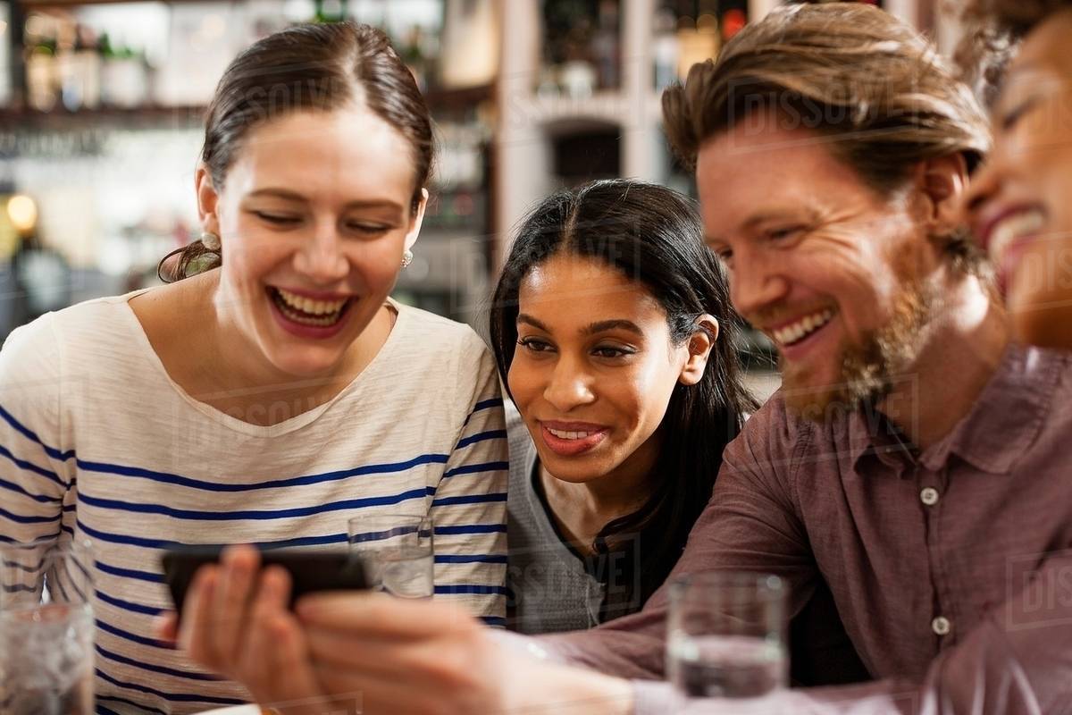 Friends at restaurant texting and showing photos using cell phones ...