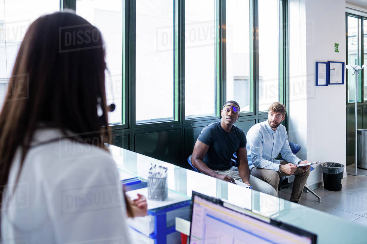 Nurse speaking with patients completing forms at hospital reception ...