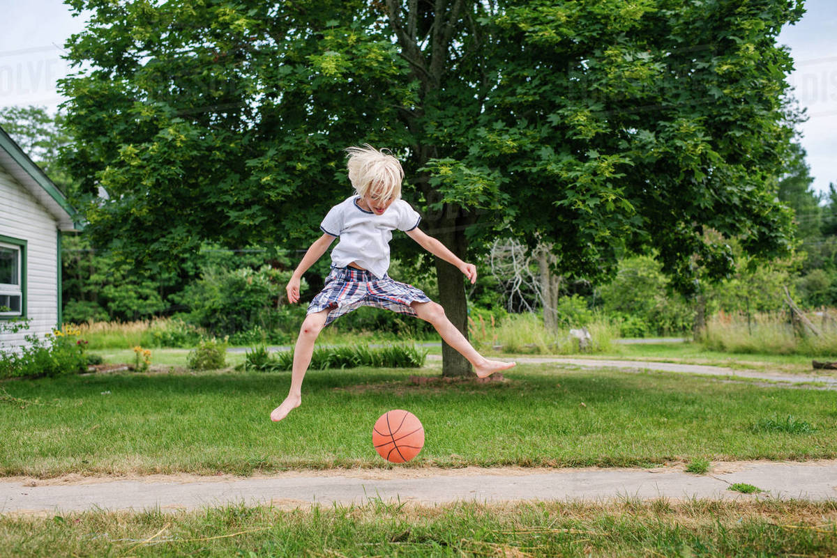 Canada, Ontario, Boy (8-9) jumping over basketball ball outdoors ...