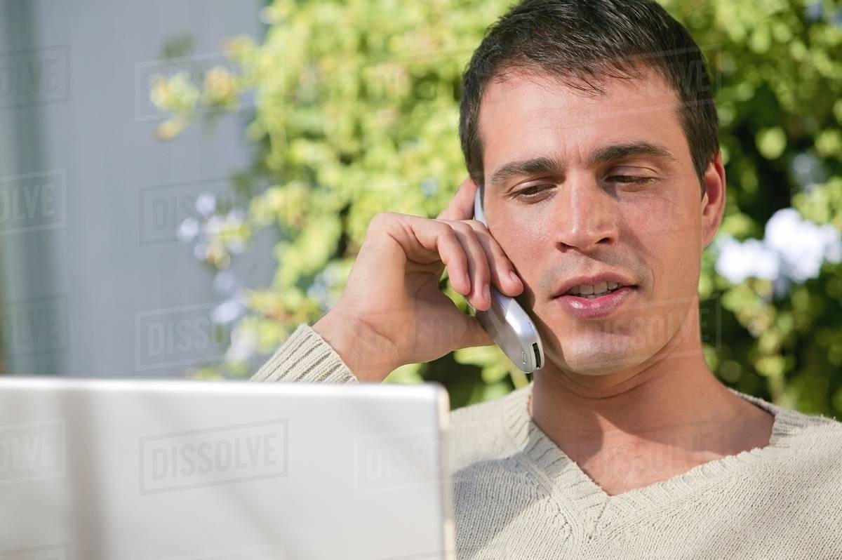Man on cellphone with laptop - Stock Photo - Dissolve