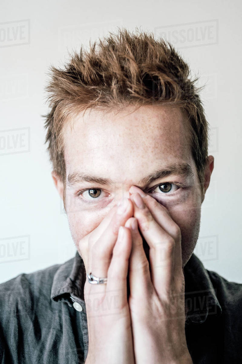 Studio portrait of young man covering mouth - Stock Photo - Dissolve