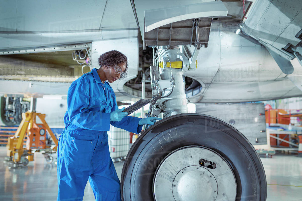 Female aircraft maintenance engineer underneath jet with digital tablet ...