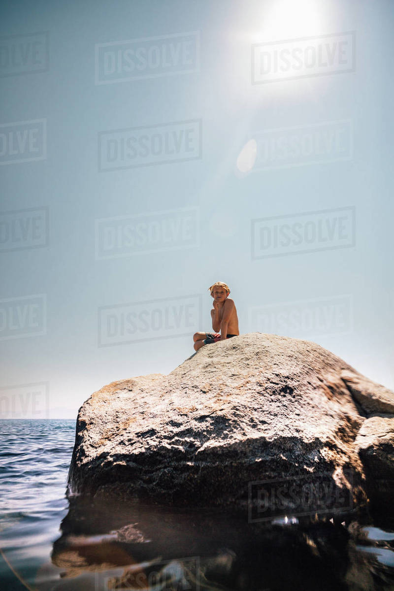 USA, California, Portrait of boy (8-9) sitting on boulder in Lake Tahoe ...