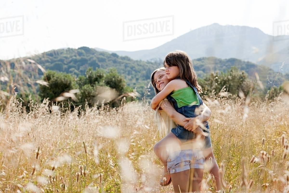 Girl carrying friend in field - Royalty-free Stock Photo | Dissolve