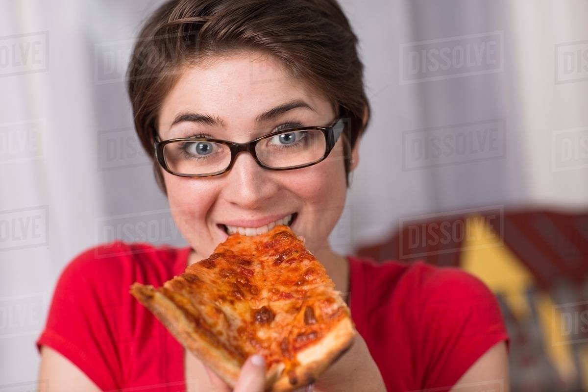Young woman eating a slice of pizza - Stock Photo - Dissolve