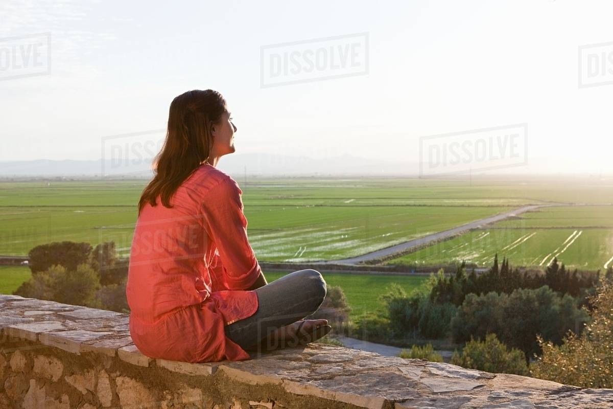 Young woman sitting on stone wall - Royalty-free Stock Photo | Dissolve