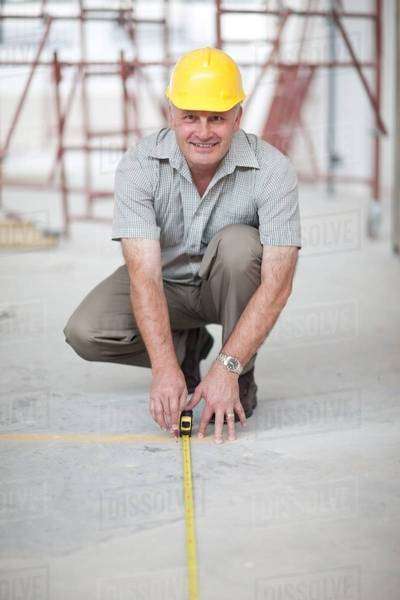 Builder measuring floor space on construction site - Stock Photo - Dissolve