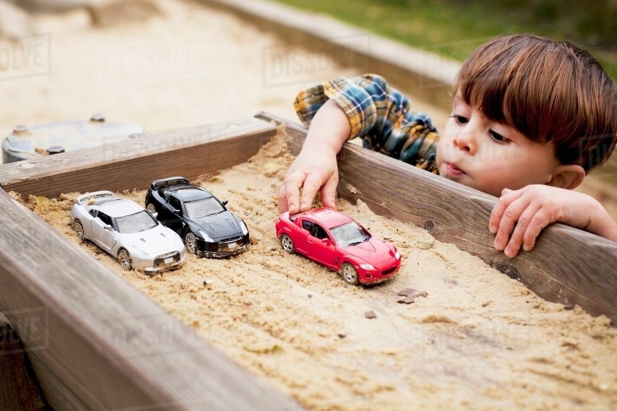 Male toddler reaching to play with toy cars in sandpit - Royalty-free ...