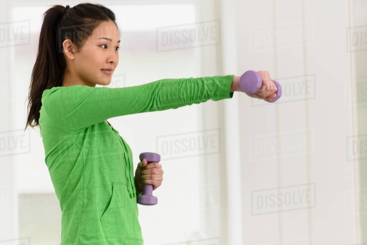 Woman lifting dumbbell with one arm forward - Stock Photo - Dissolve