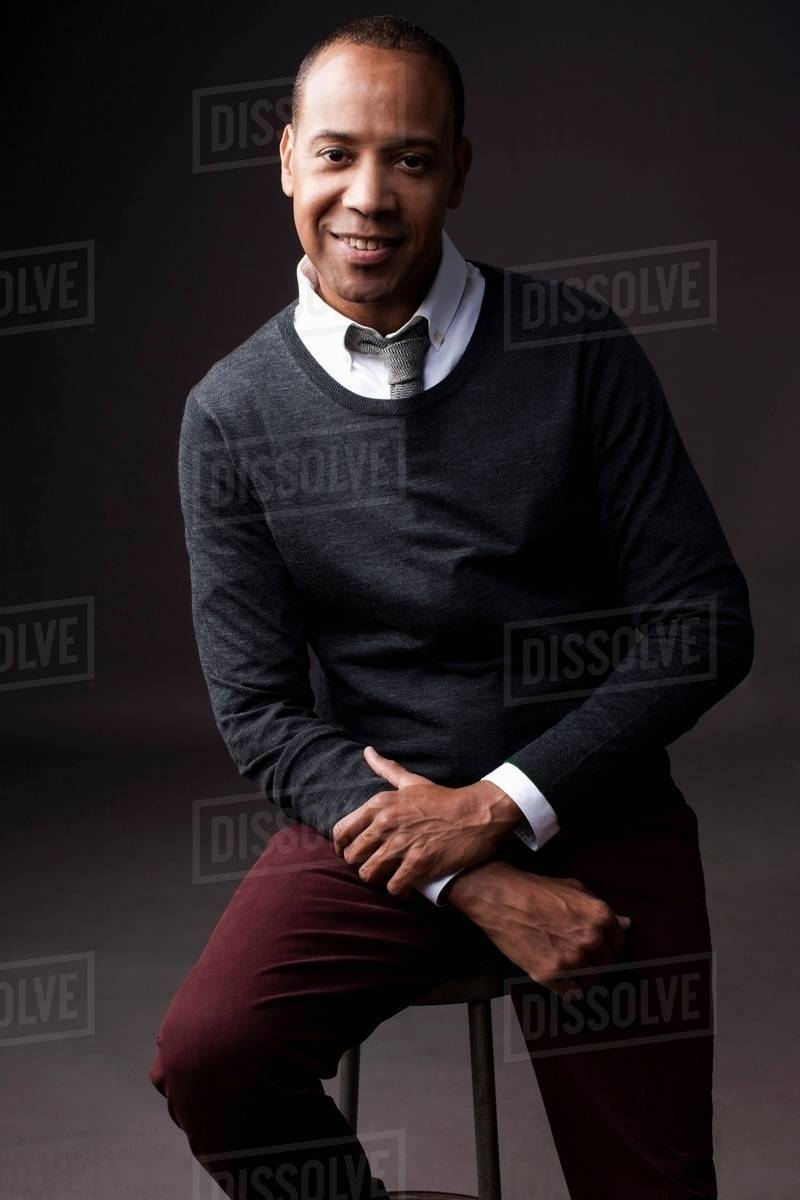 Smiling man sitting on stool - Stock Photo - Dissolve