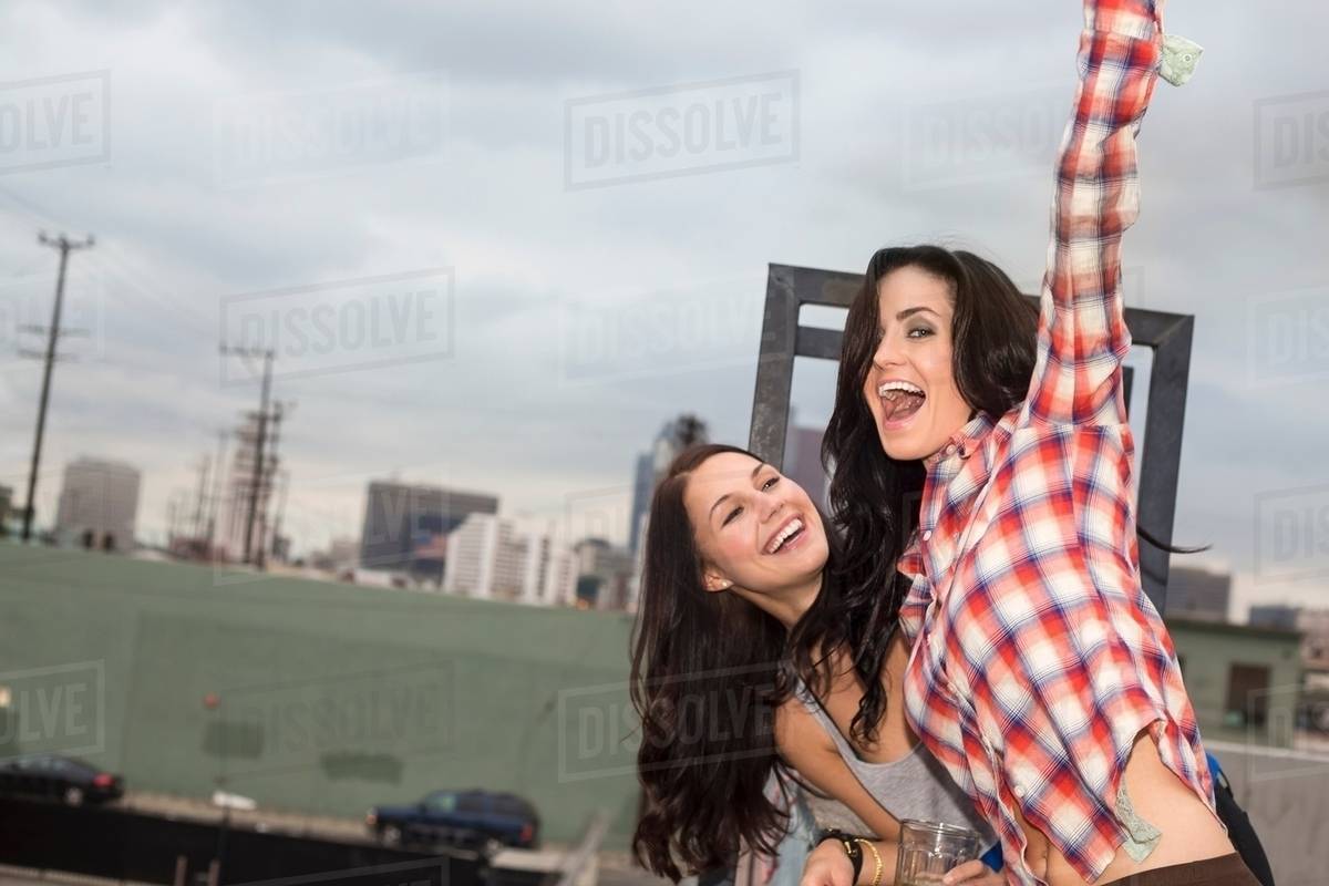 Two female friends jumping around at rooftop party - Stock Photo - Dissolve