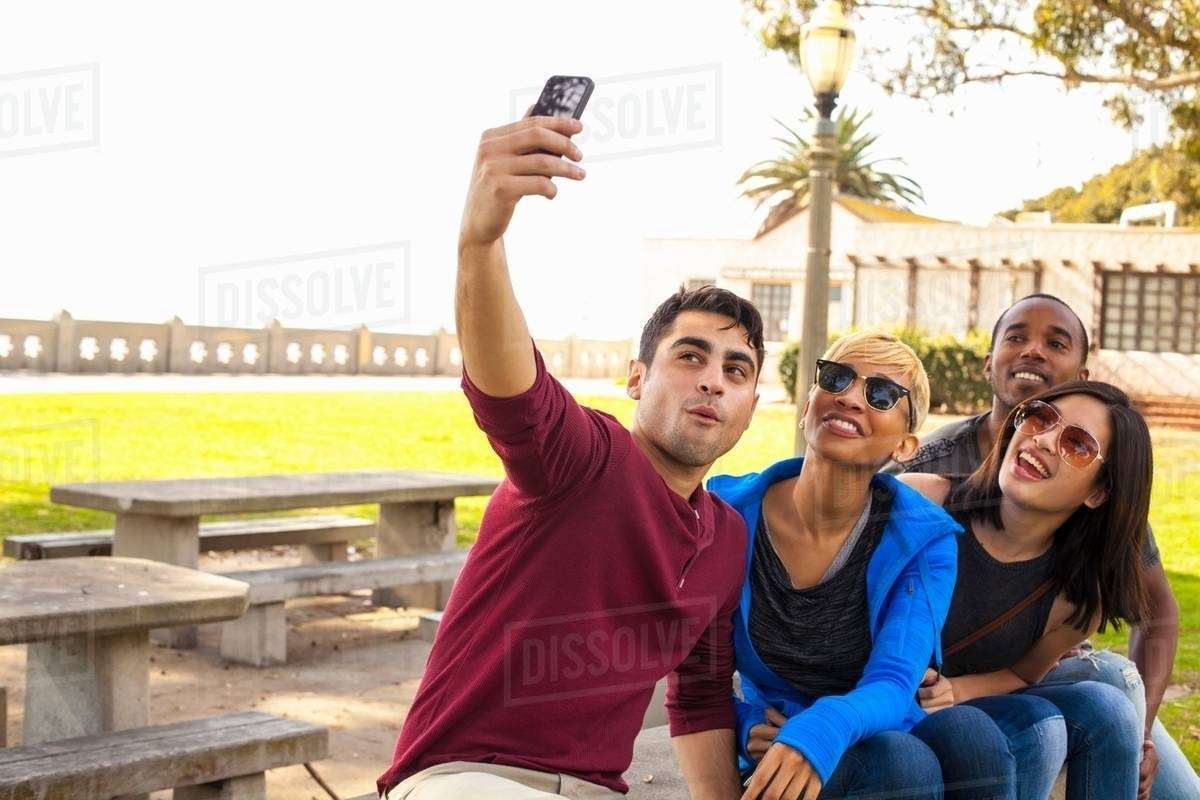 Group of friends sitting together, taking self portrait with smartphone ...