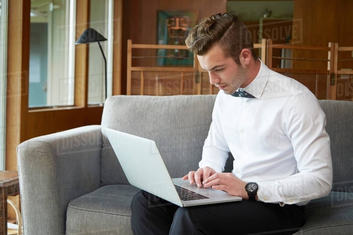 Portrait of man sitting on sofa working from laptop - Royalty-free ...