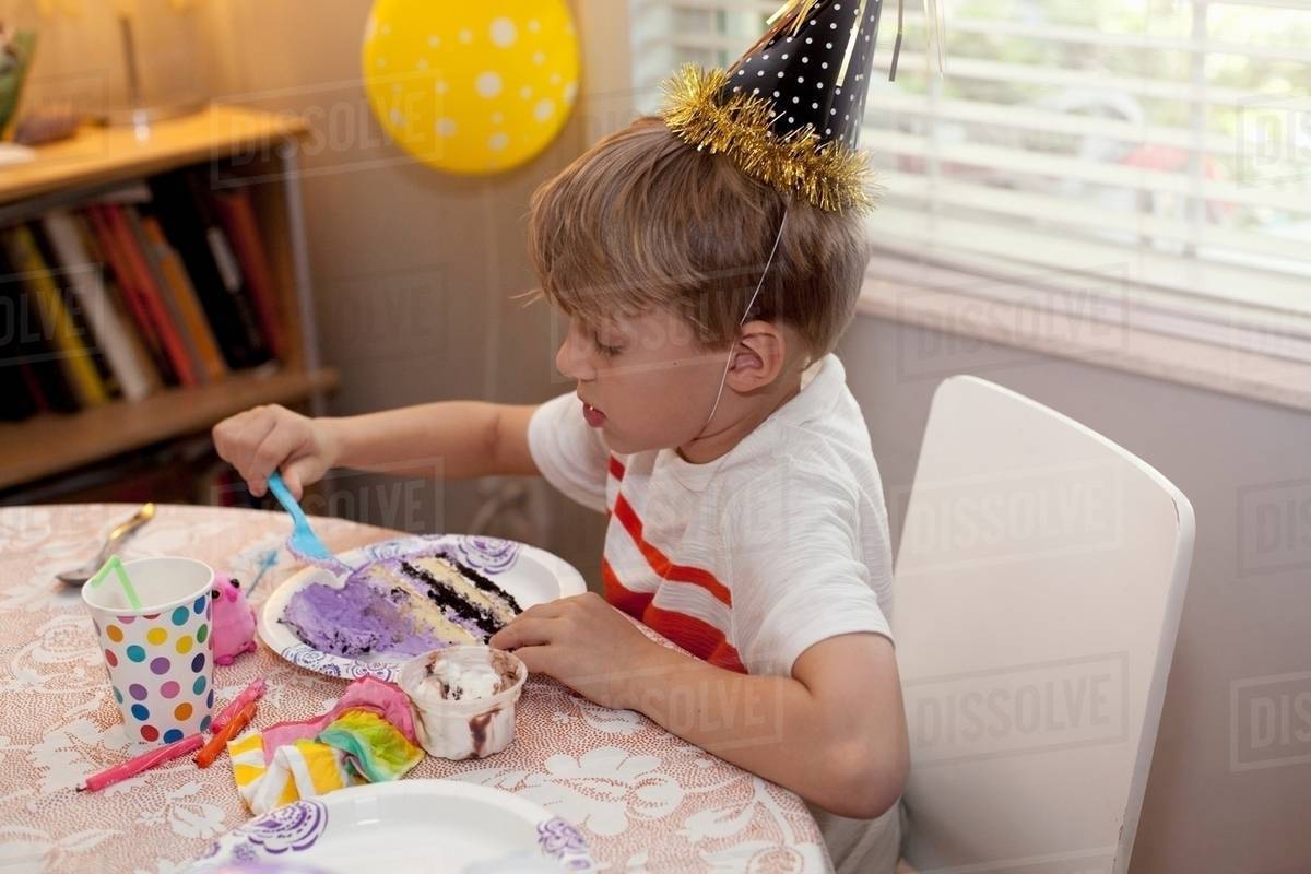 Boy in party hat sitting at table eating birthday cake - Royalty-free ...
