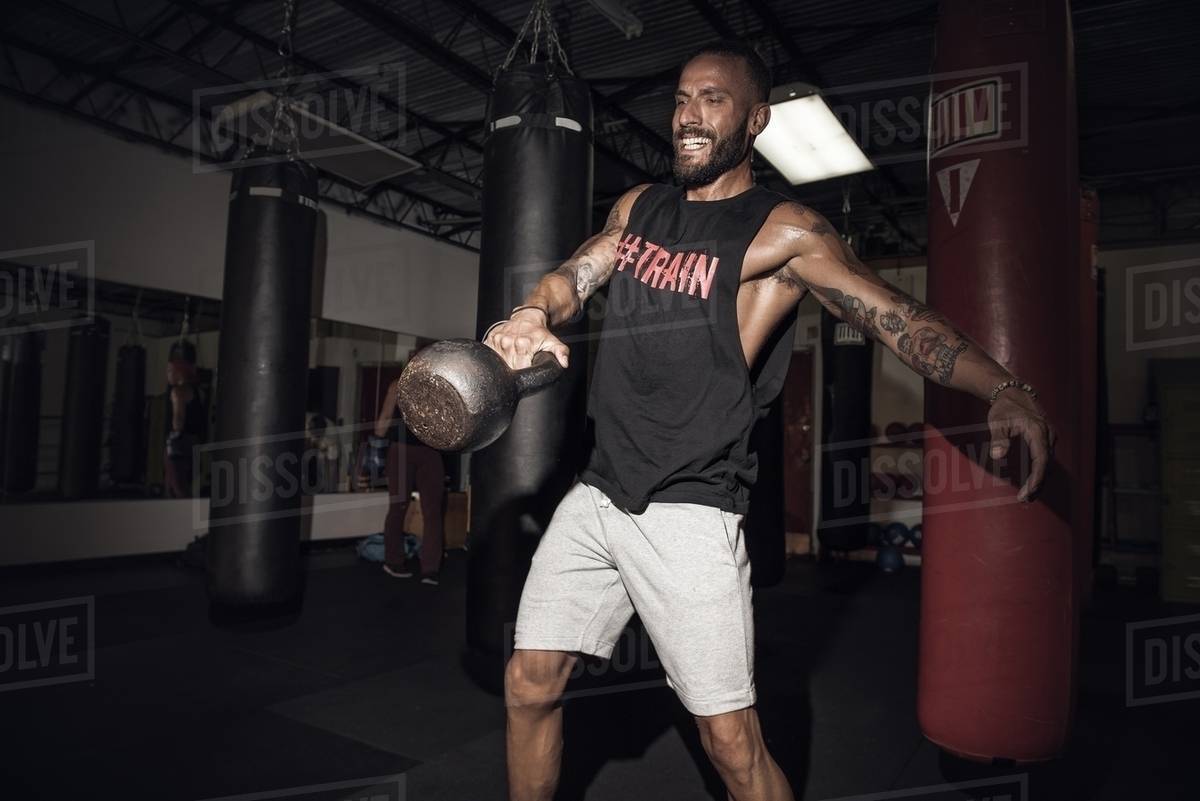 Male boxer lifting kettlebell with gritted teeth in gym - Stock Photo ...