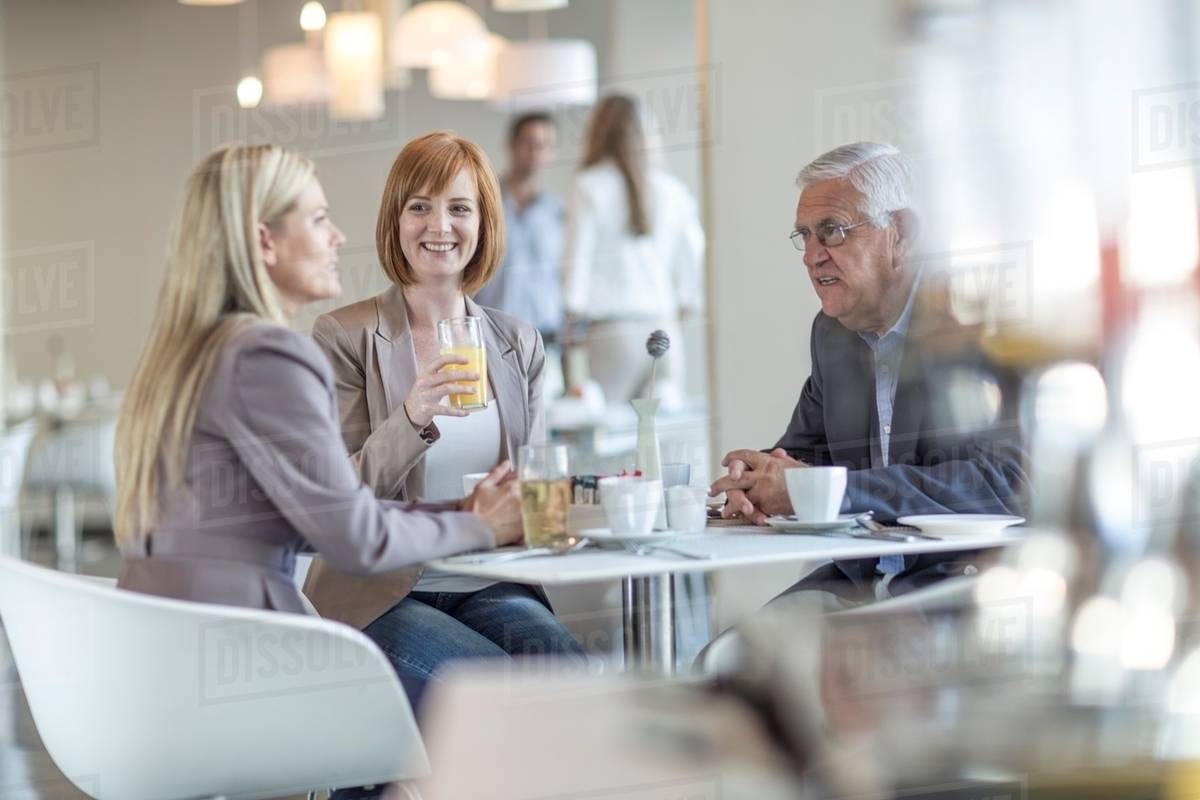 Senior businessman talking to team at breakfast table in hotel ...