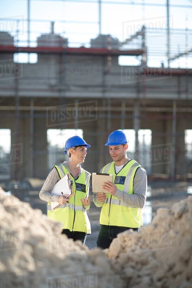 Surveyor using digital tablet talking to builder on construction site ...
