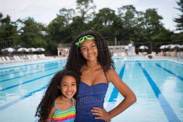 Sisters wearing swimsuits standing in front of swimming pool, looking ...