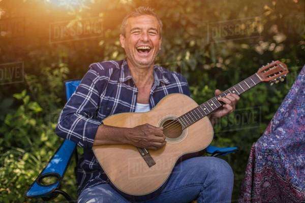 Portrait of mature man singing and playing acoustic guitar whilst ...