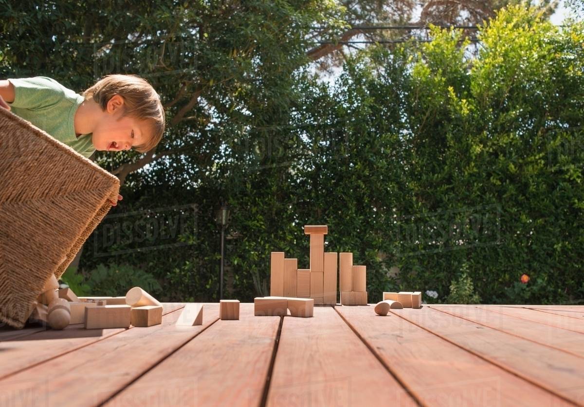 Young boy tipping wooden building blocks out on garden decking ...