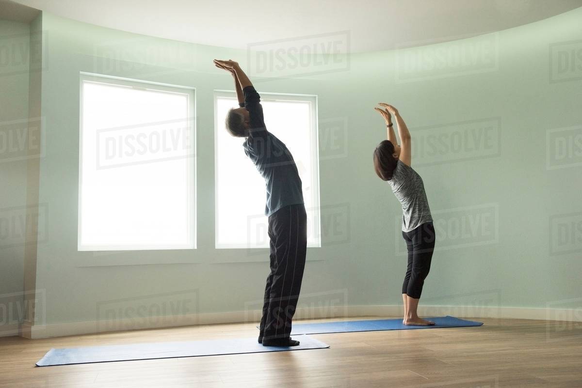 Side view of mature couple reaching upwards stretching arms bending ...