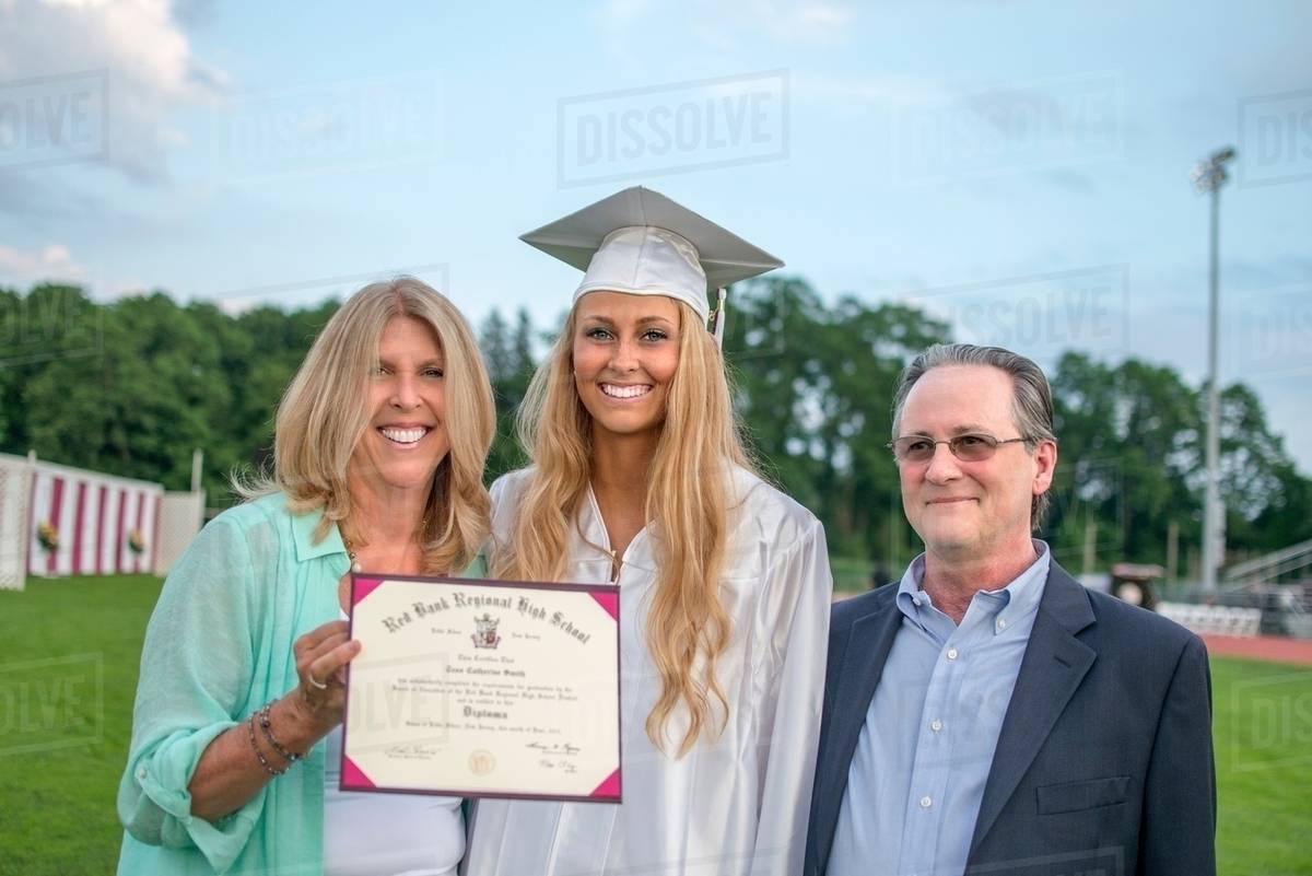Portrait of young female graduate with parents at graduation ceremony ...