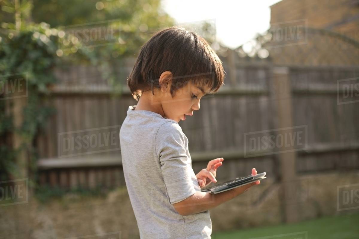Side view of boy in garden looking down using digital tablet - Stock ...