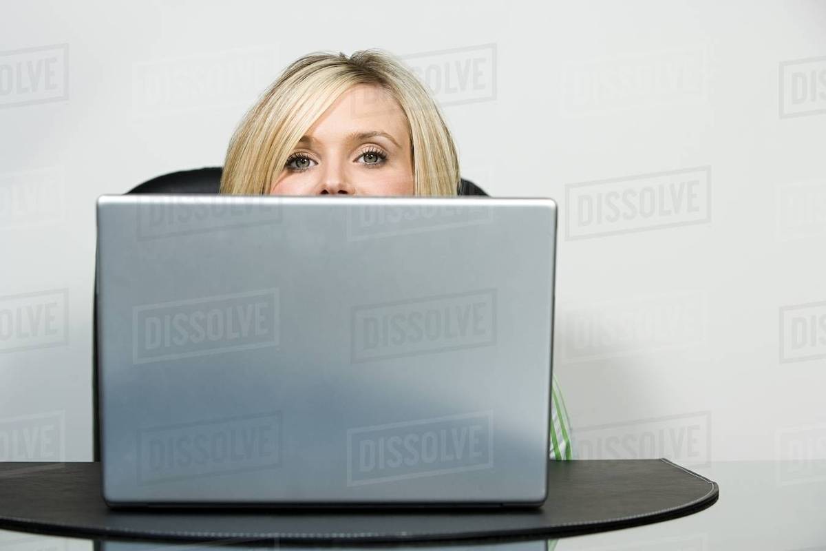 An office worker peeking over a laptop - Stock Photo - Dissolve