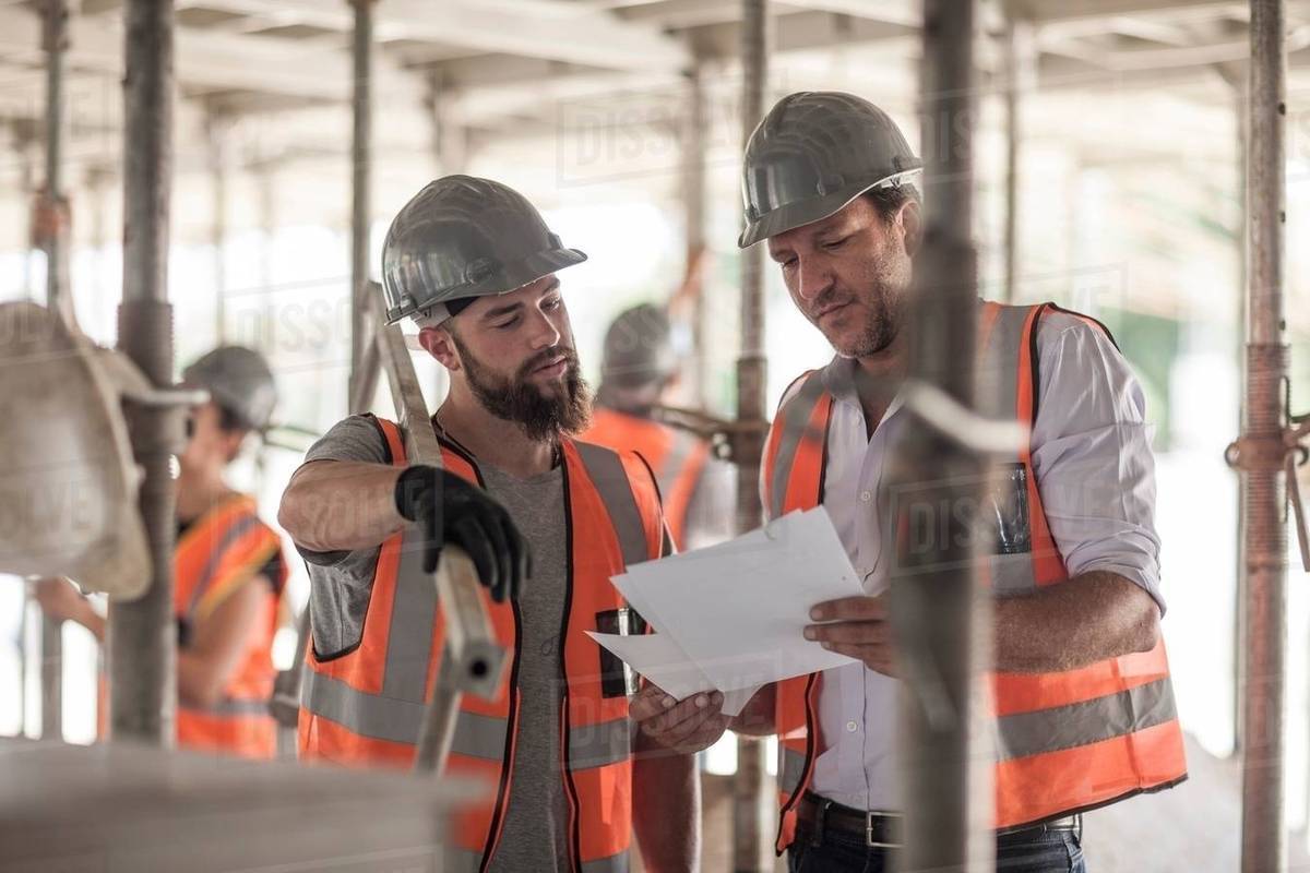 Male builders looking at blueprint on construction site - Royalty-free ...