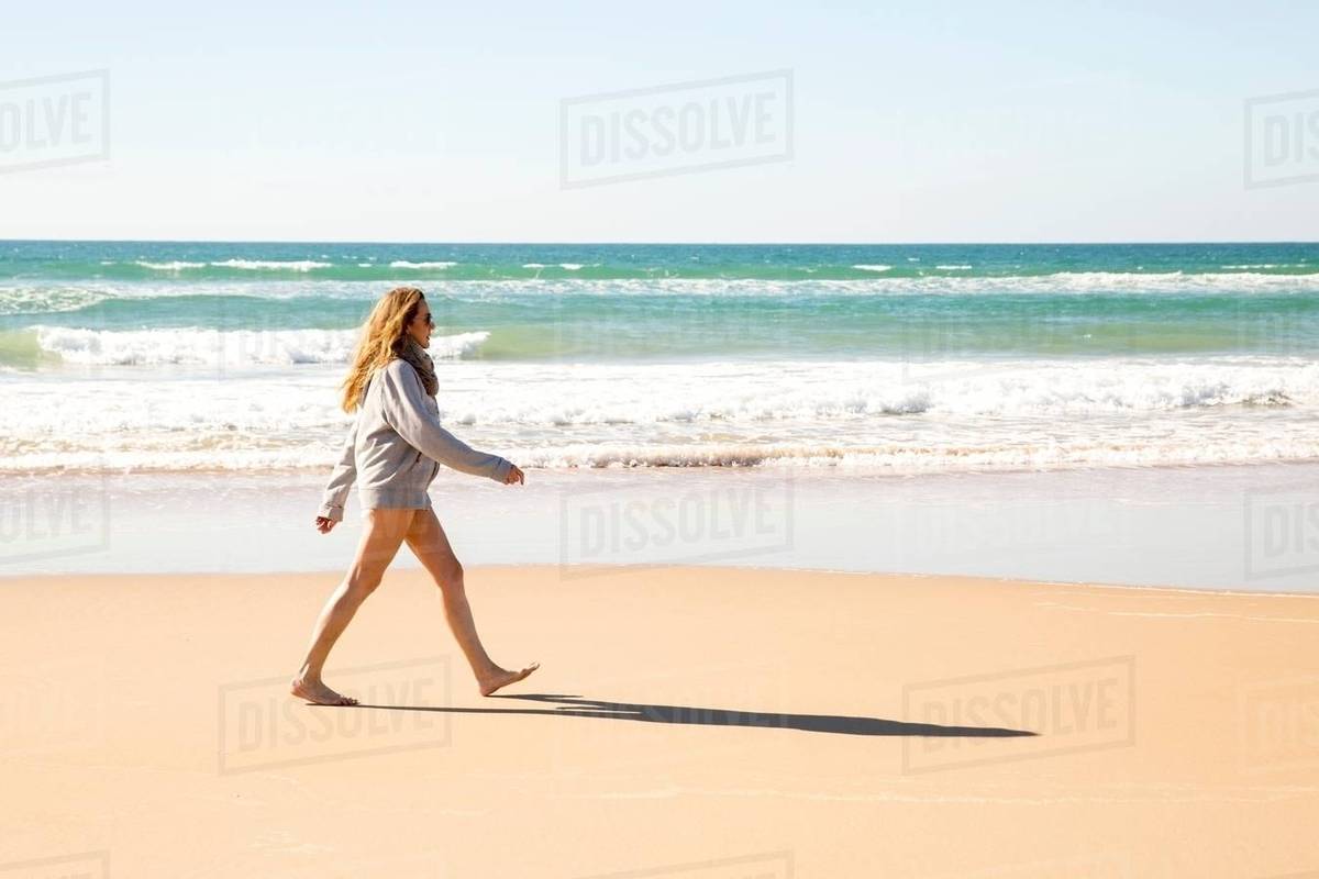 Bare legged woman wearing hoody striding out on beach, Conil de la ...