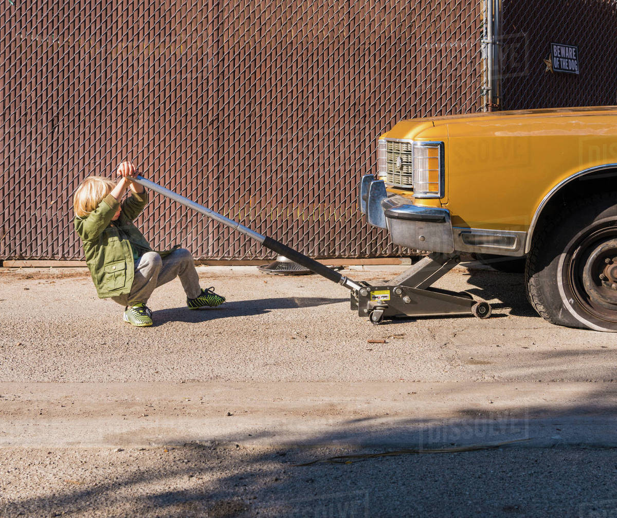 Boy using car jack to raise car - Royalty-free Stock Photo | Dissolve