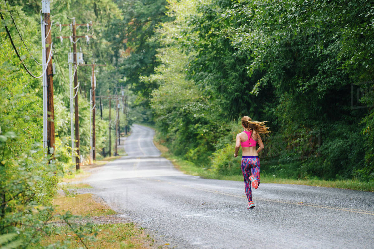 Rear view of teenage female runner running down rural road - Royalty ...