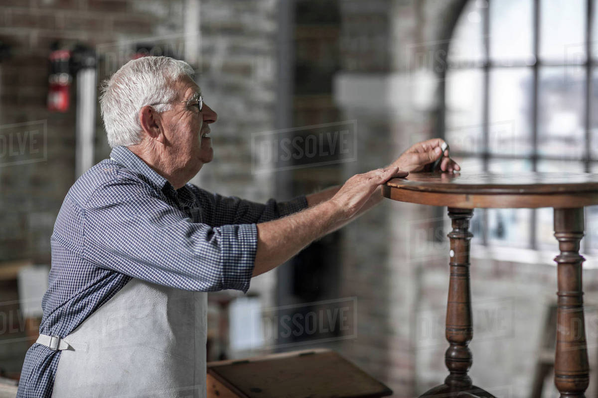 Senior craftsman inspecting table in antique restoration workshop ...