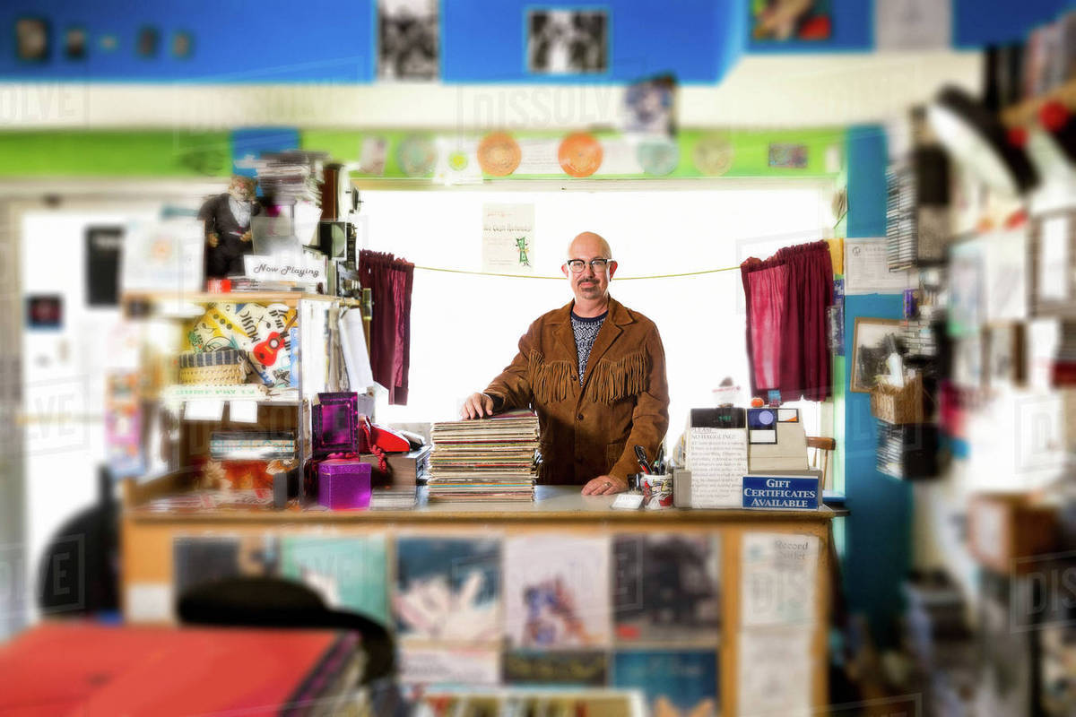 Portrait of mature man in record shop, leaning on stack of records ...