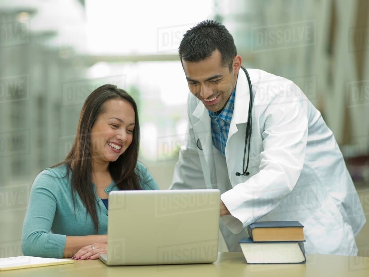 Mid adult doctor using laptop with young student, smiling - Royalty ...