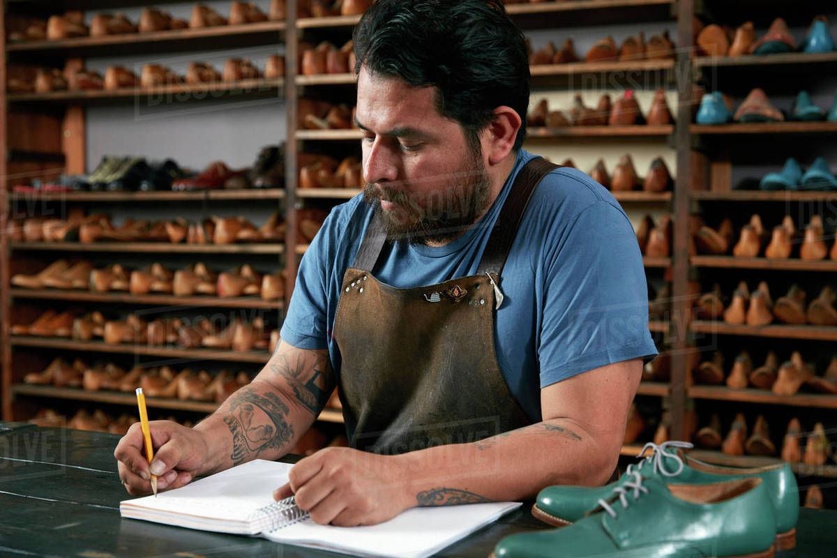 Male cobbler in traditional shoe shop making notes on green brogues ...
