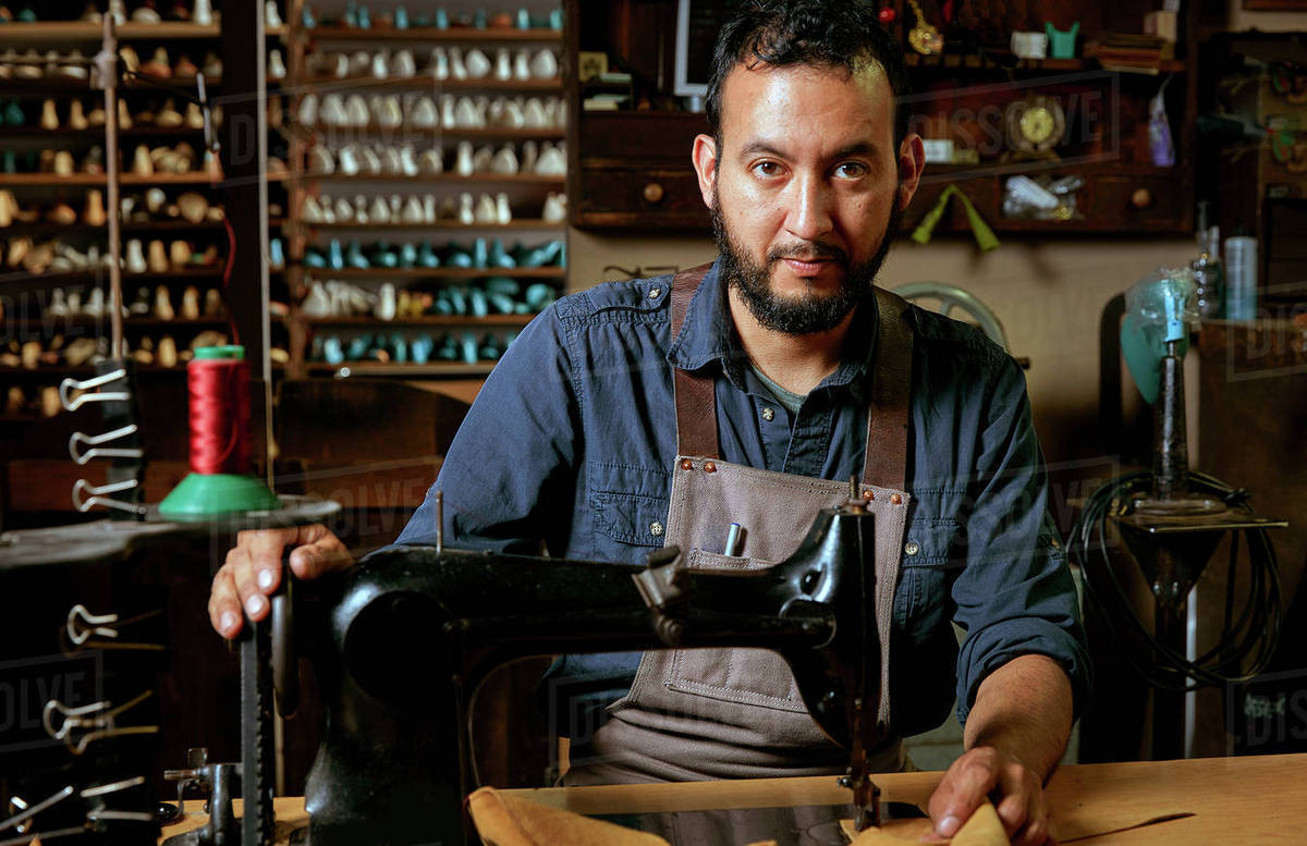 Portrait of male cobbler at sewing machine in traditional shoe workshop ...