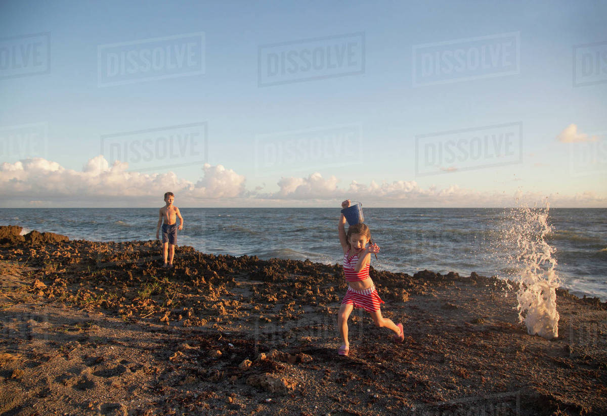Girl running away from splashing wave on beach, Blowing Rocks Preserve ...