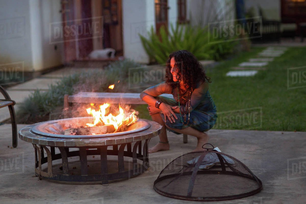 Mature woman crouching in front of patio fire at dusk - Royalty-free ...
