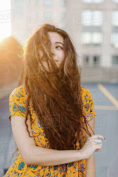 Portrait of young girl pulling long wavy hair across face in parking ...