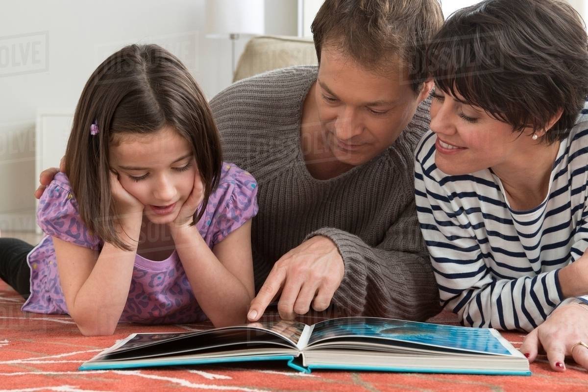 Daughter looking at picture book with parents - Stock Photo - Dissolve