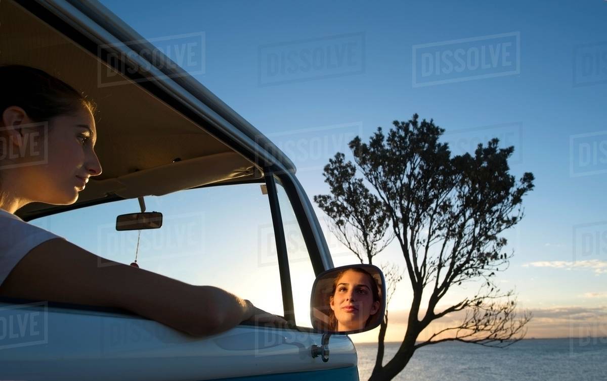 Young woman looking out of camper van window at dusk - Royalty-free ...